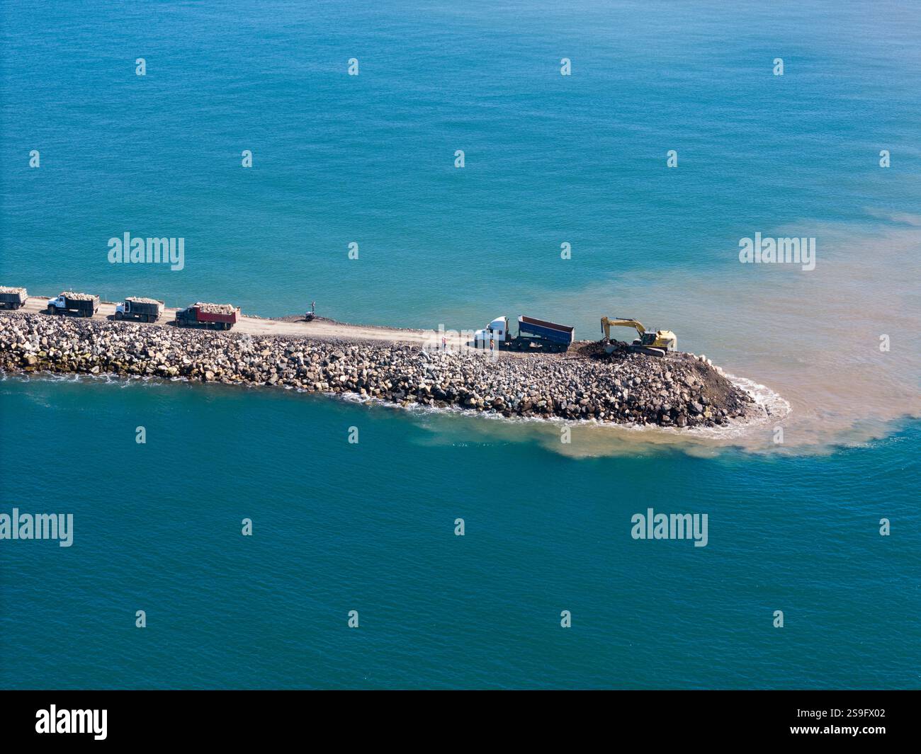 Excavator load stones from lorry carrier on sea water background aerial ...