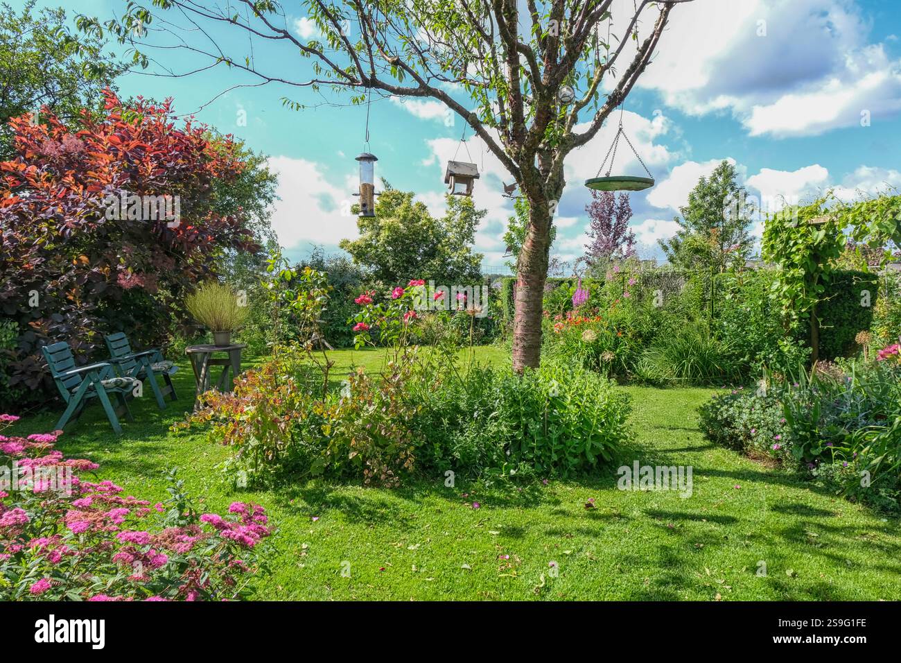 Lovely june garden with plants, flowers, chairs and bird feeders Stock ...