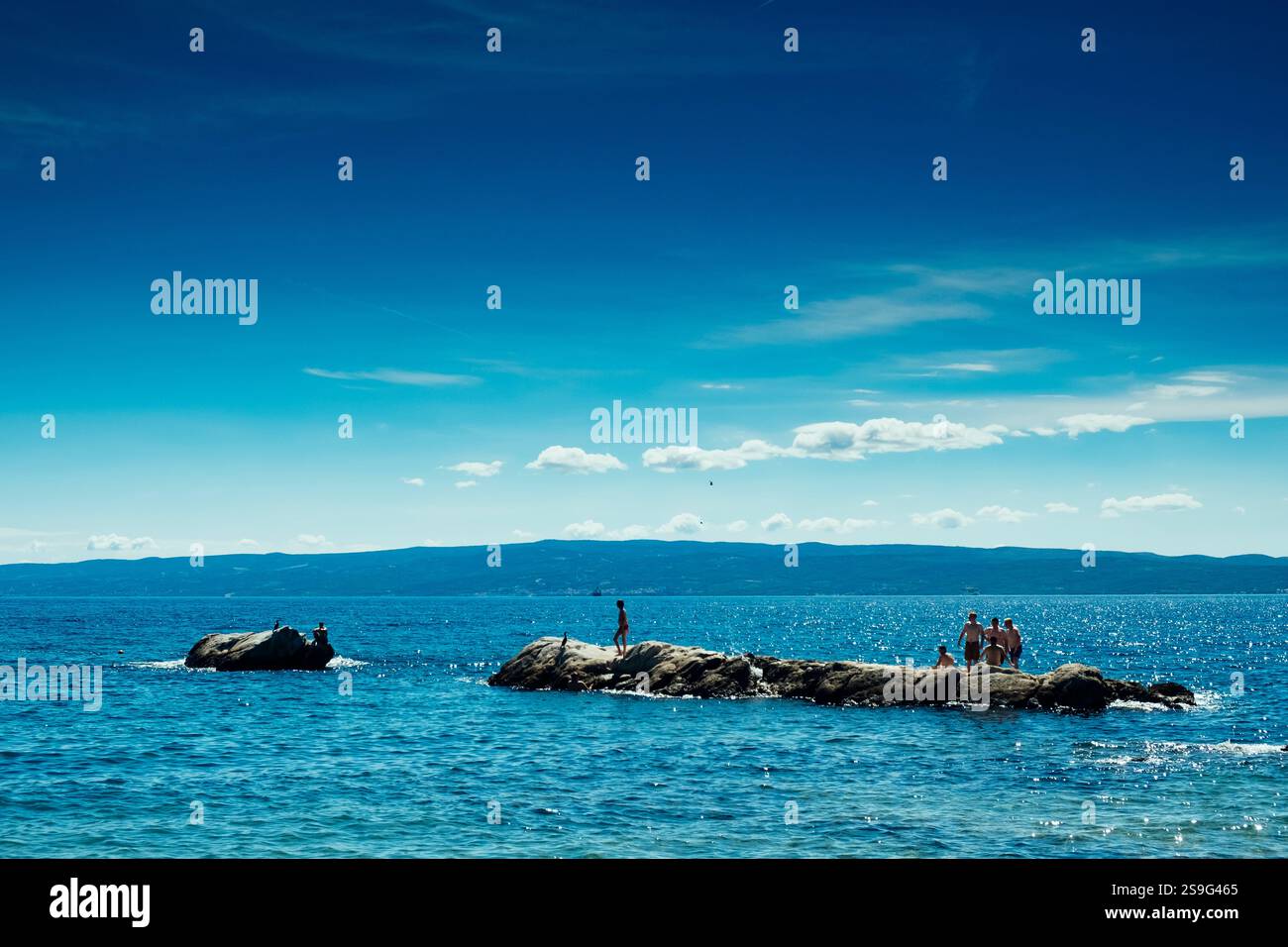 Swimmers standing on a rock at at Uvala Firule beach, Split, Croatia ...