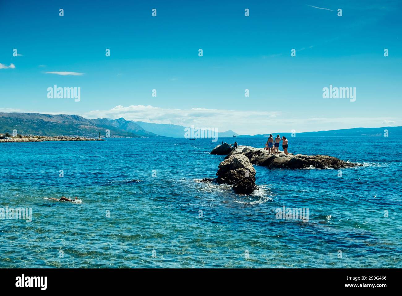 Swimmers standing on a rock at at Uvala Firule beach, Split, Croatia ...