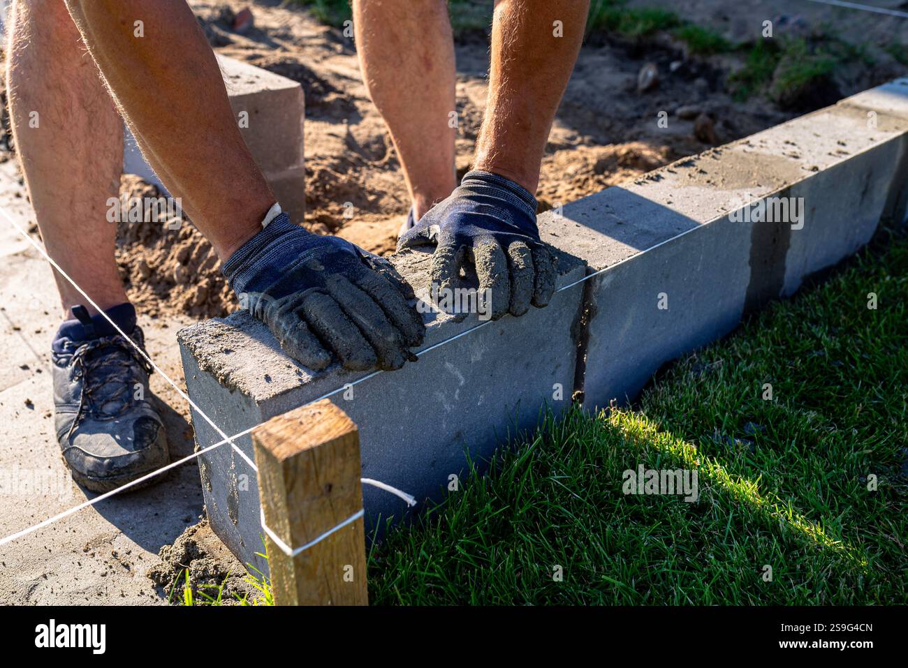 A man lays concrete blocks on a poured foundation, gluing them with ...