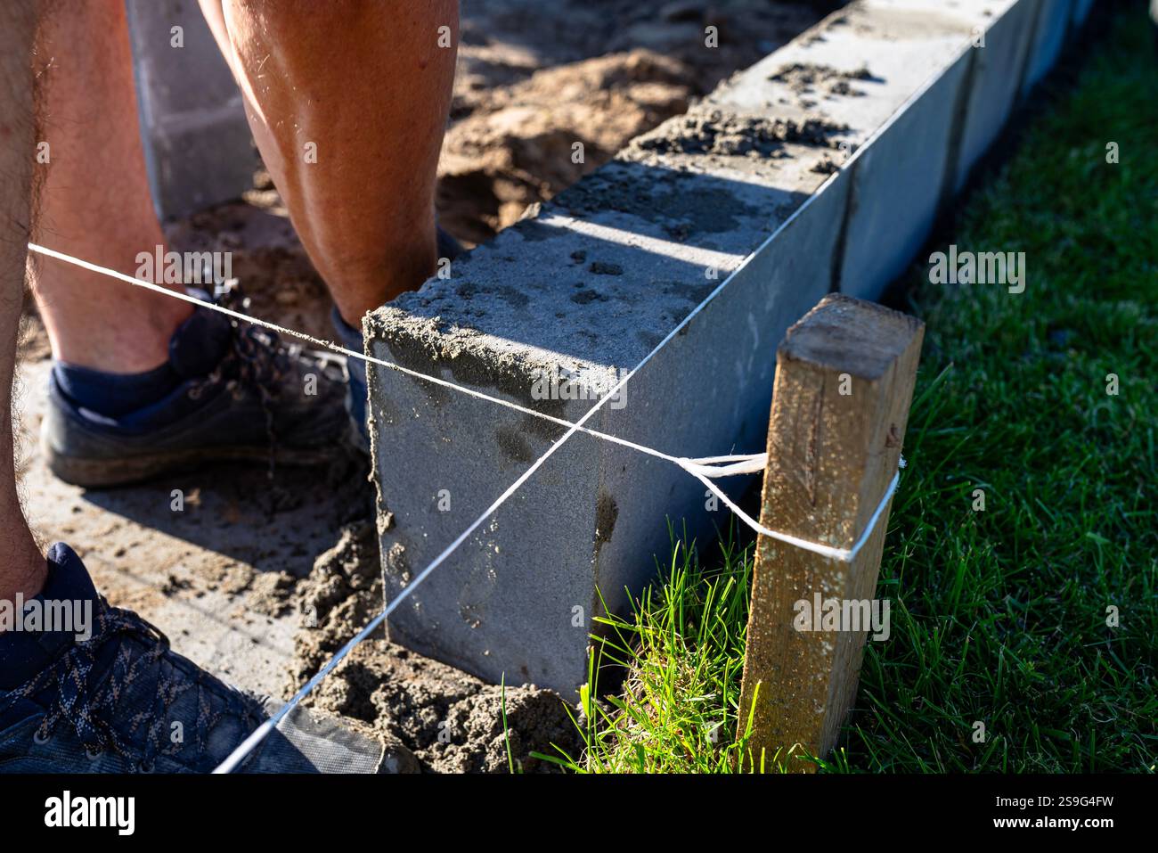 A man lays concrete blocks on a poured foundation, gluing them with ...