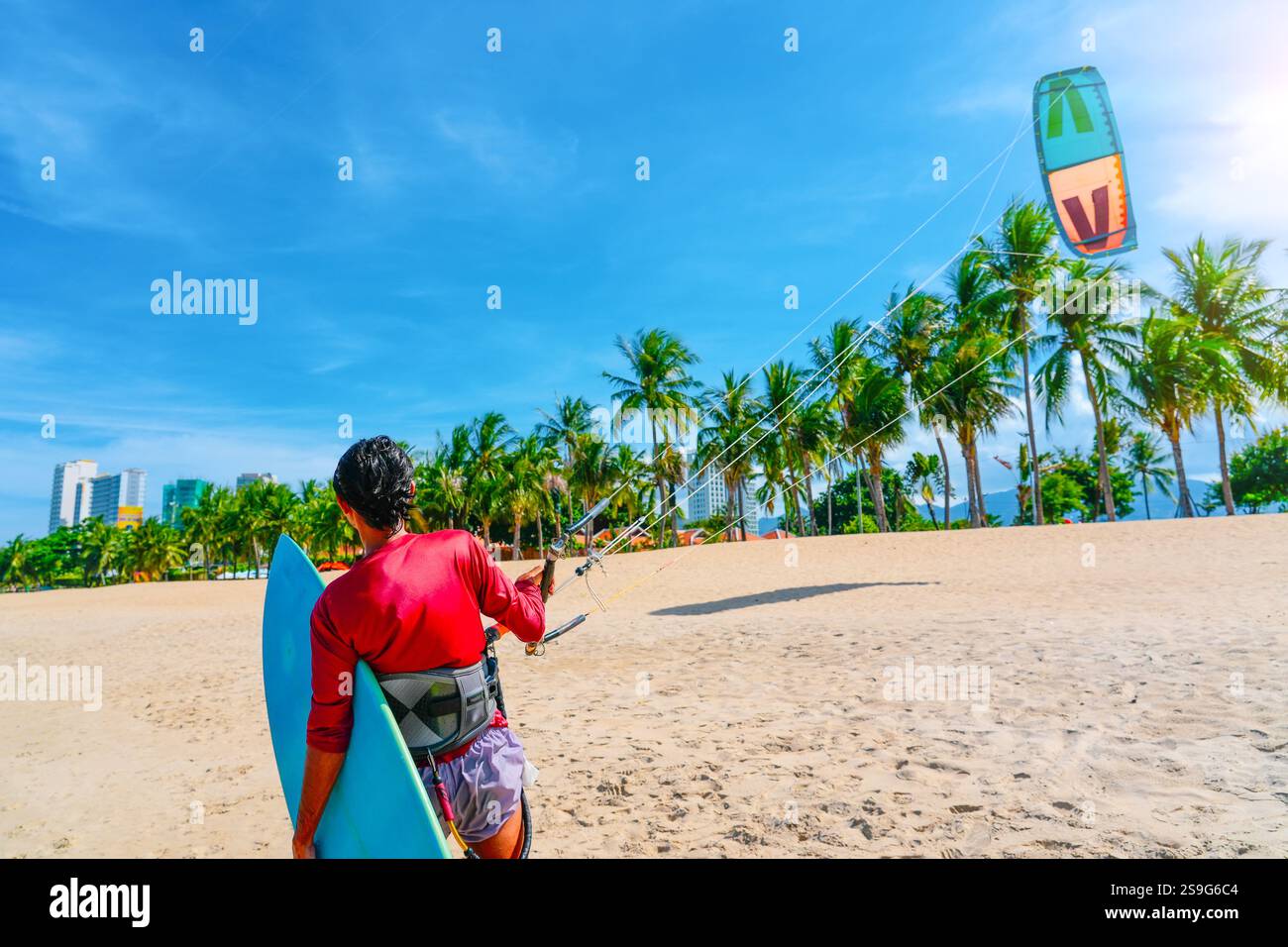 kite surfer stands on the sandy beach, holding a surfboard while ...