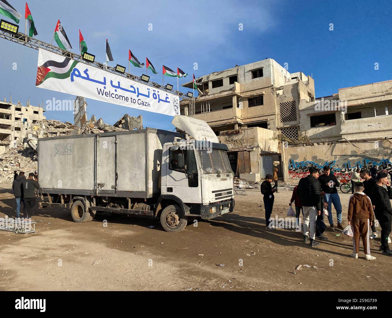 People gather by a banner welcoming people near the rubble of a ...