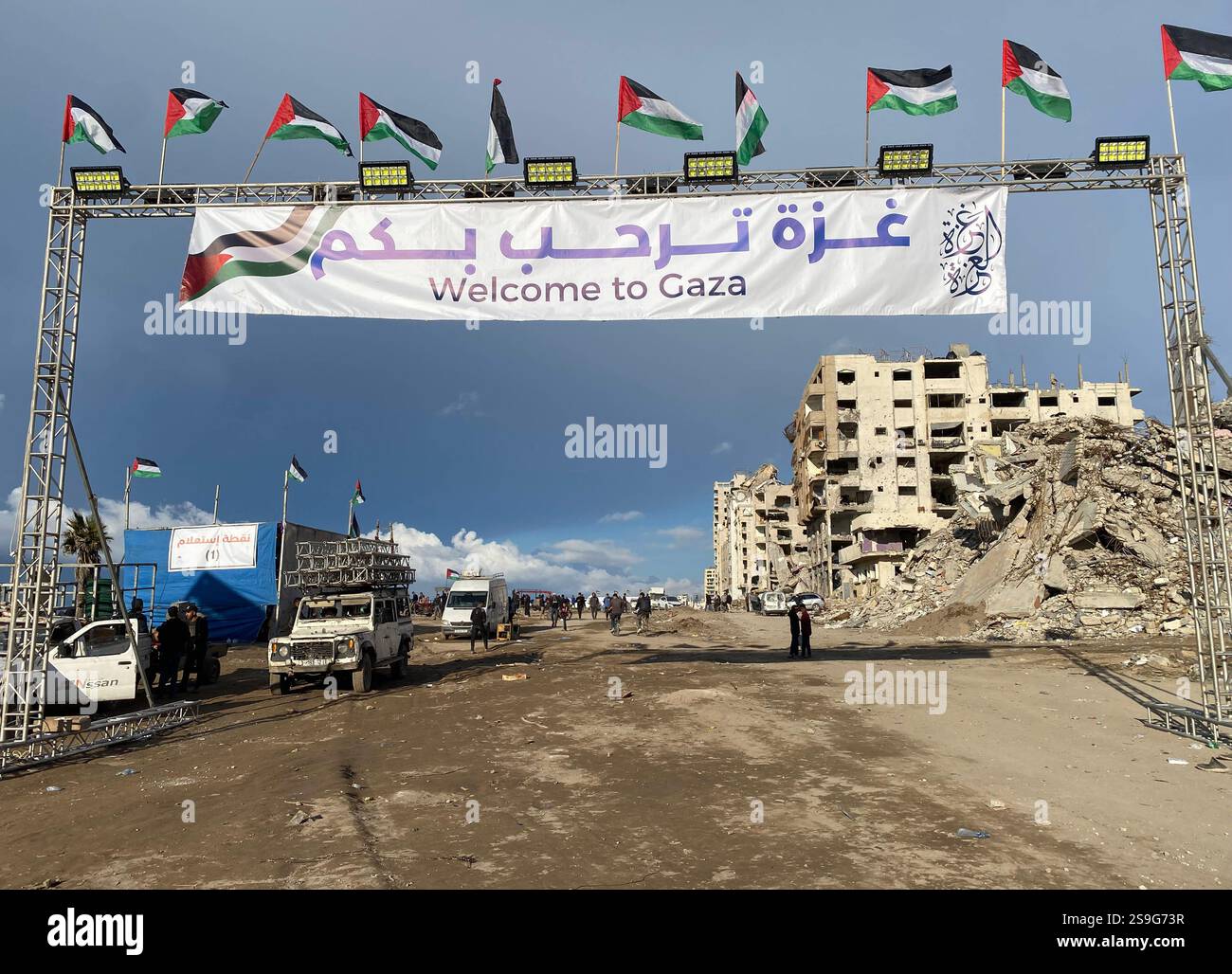 People gather by a banner welcoming people near the rubble of a ...