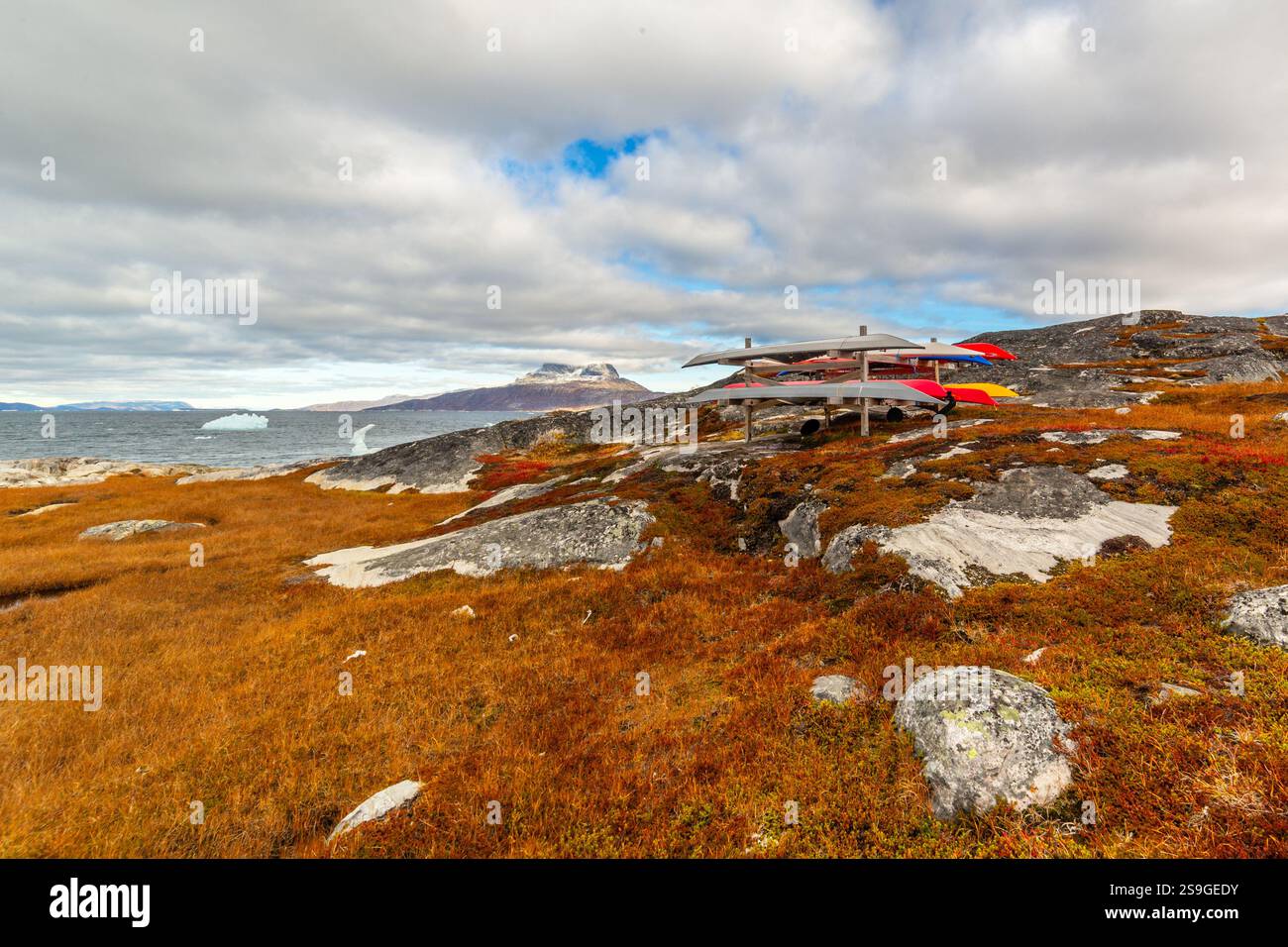 Orange tundra landscape with fjord and rows of stored Inuit kayaks ...