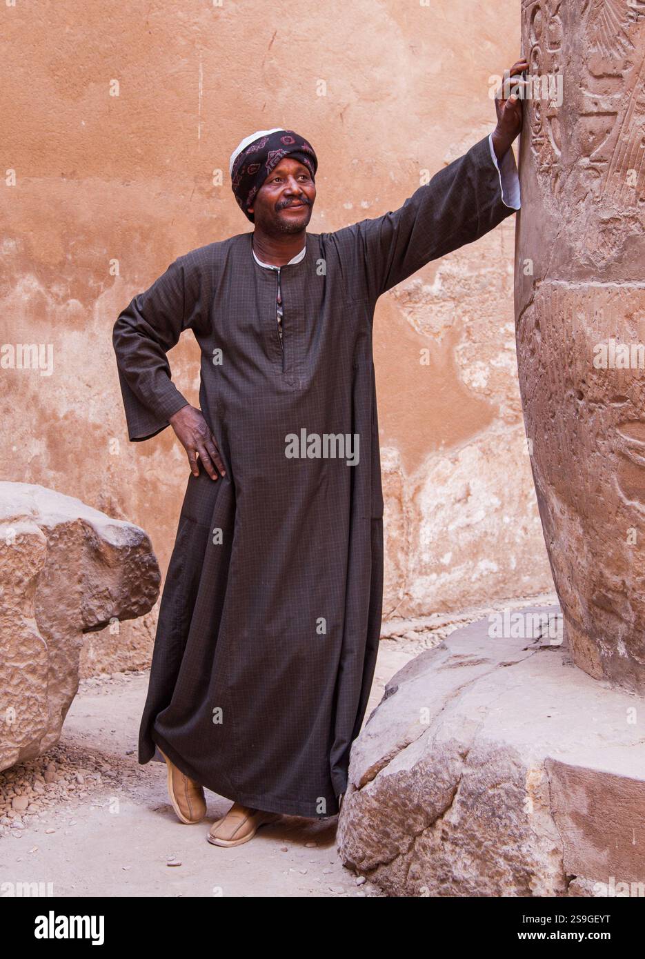 Egyptian Guide Dressed In Traditional Galabiya Waiting For Willing Tourists And Pillar With