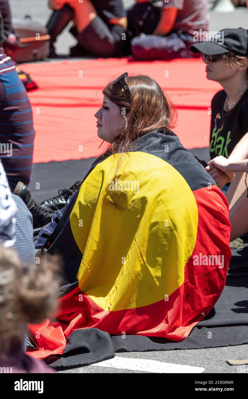A young woman draped in the Aboriginal flag sits amidst the crowd ...