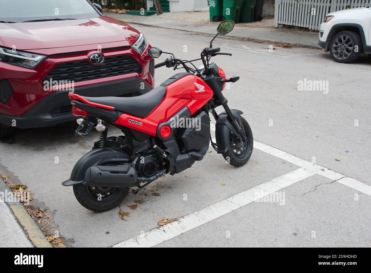 Red moped scooter parked on the side of the street in front of red SUV ...