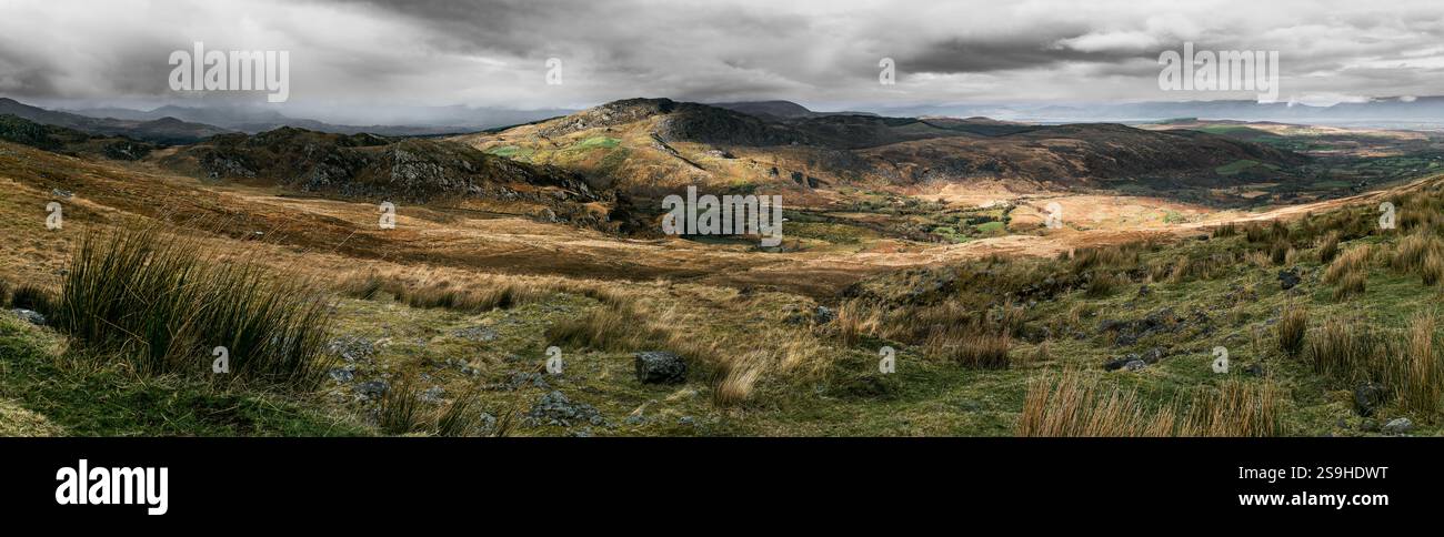 Rolling hills and mountains under a dark, brooding sky. Patches of ...