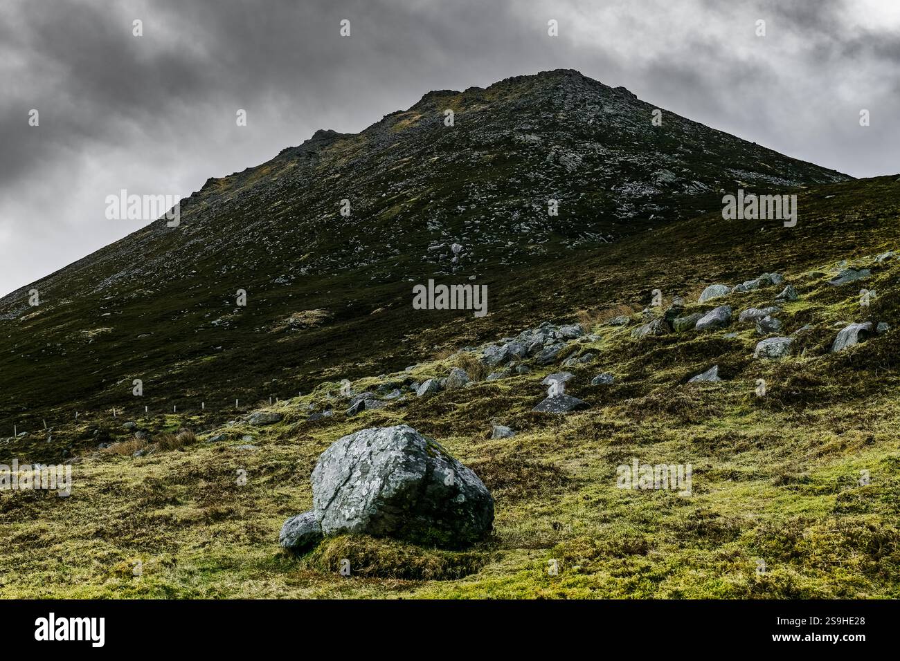 A large grey boulder rests in short, grassy terrain. A distant, green ...