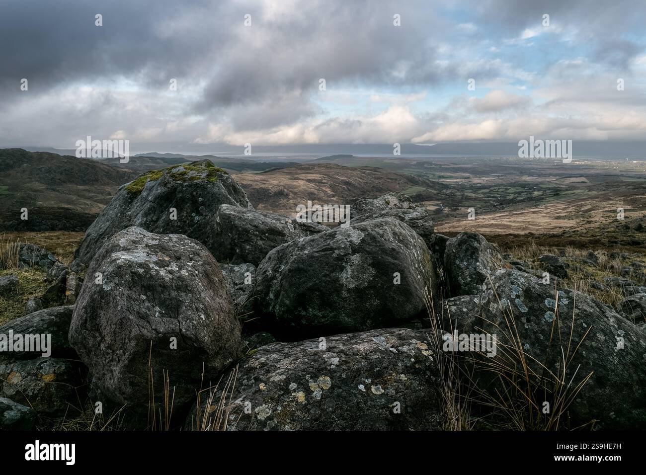 A cluster of large, dark grey rocks, lichen-covered, sits atop a grassy ...