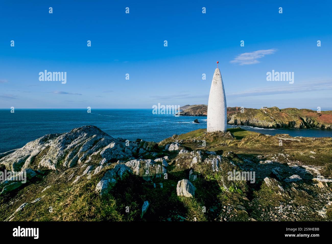 Coastal tower. A white, conical tower sits on a rocky, grassy headland ...