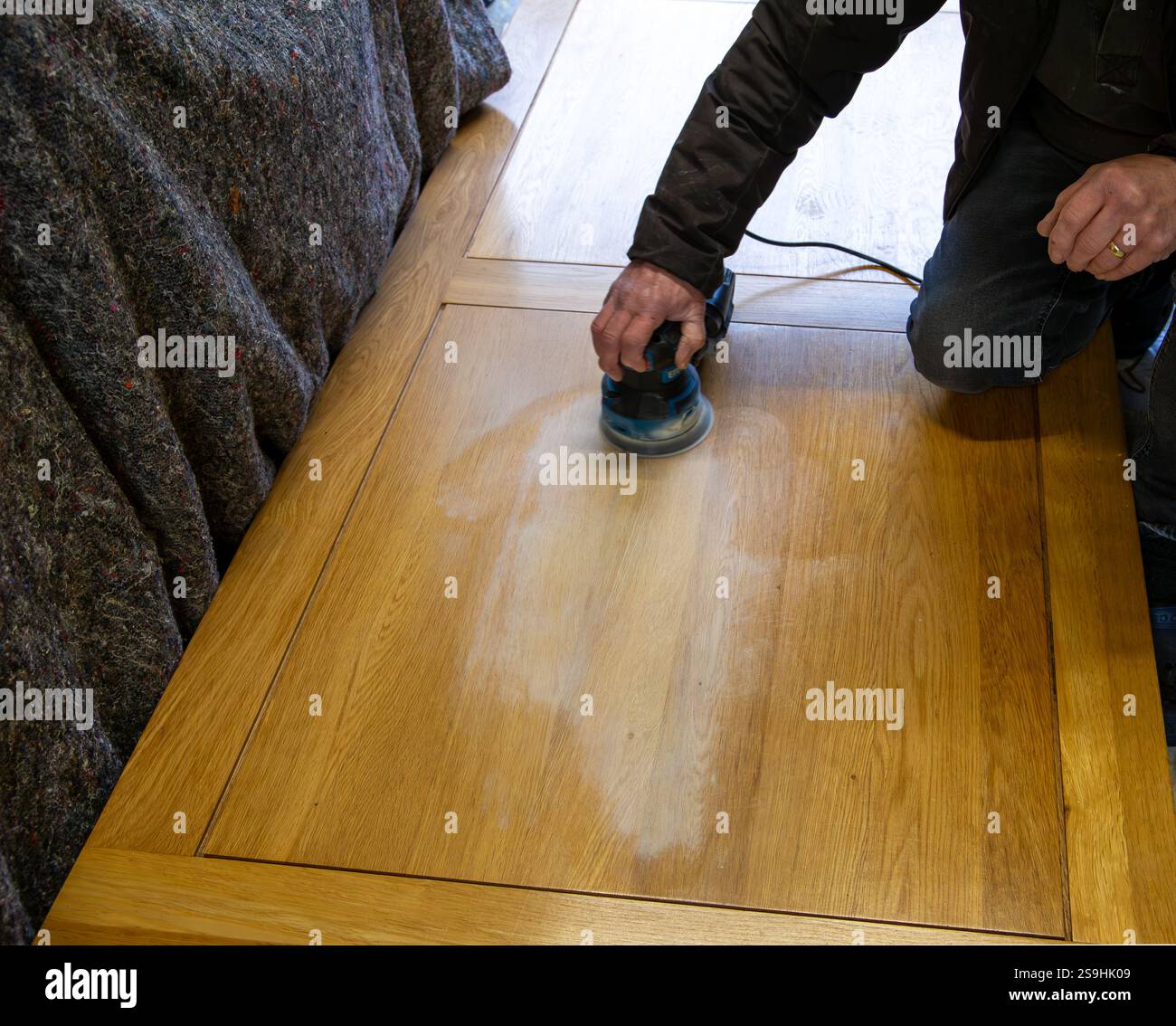 Close-up of a person sanding a wooden table surface with an electric ...