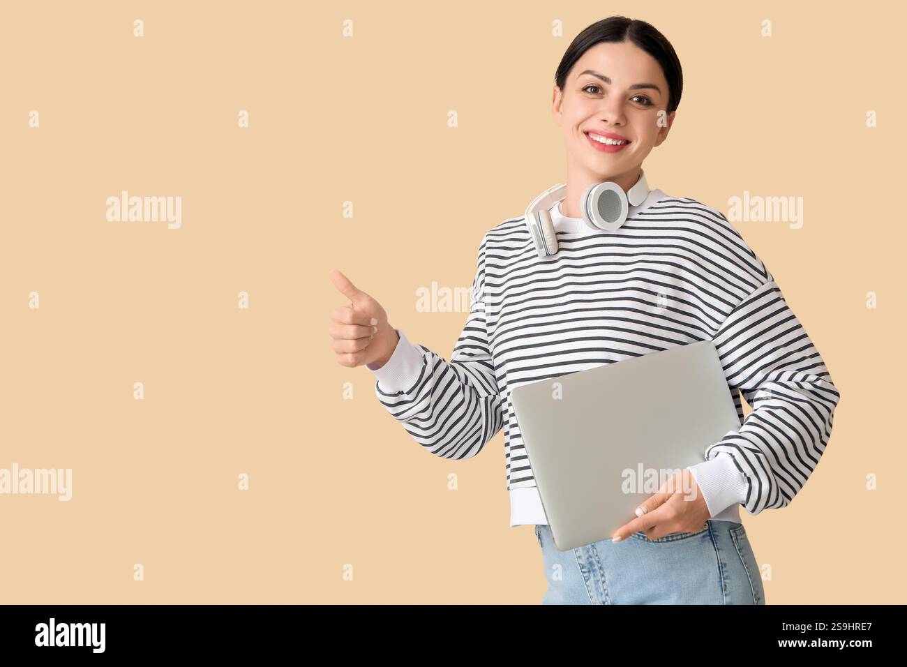 Female programmer with laptop showing thumb-up on beige background ...