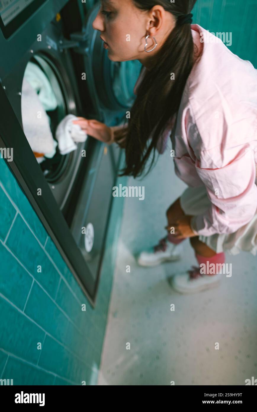 A young woman happily doing laundry in a chic, vibrant laundromat ...
