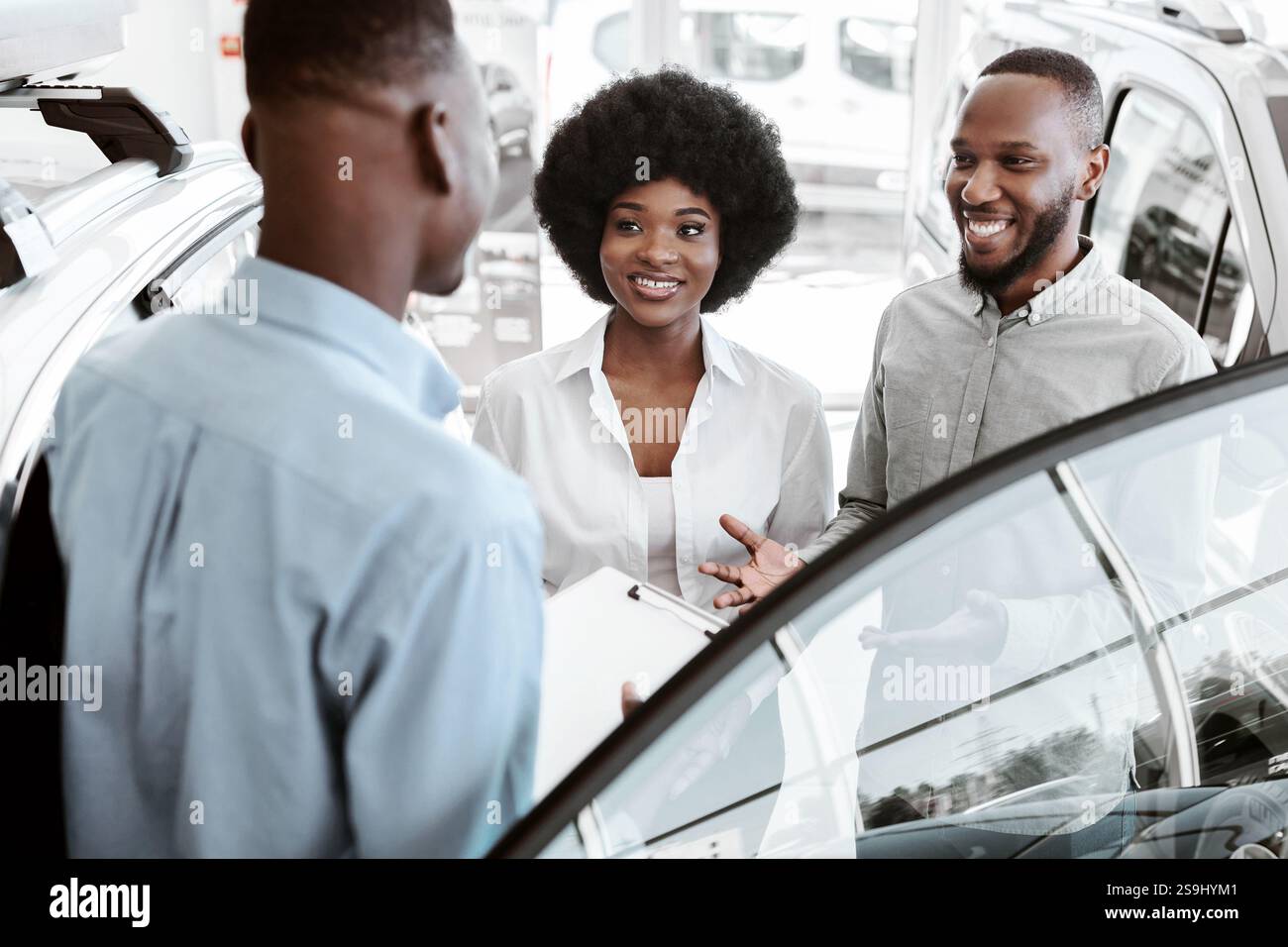 Young black couple selecting new car at auto dealership, salesman ...