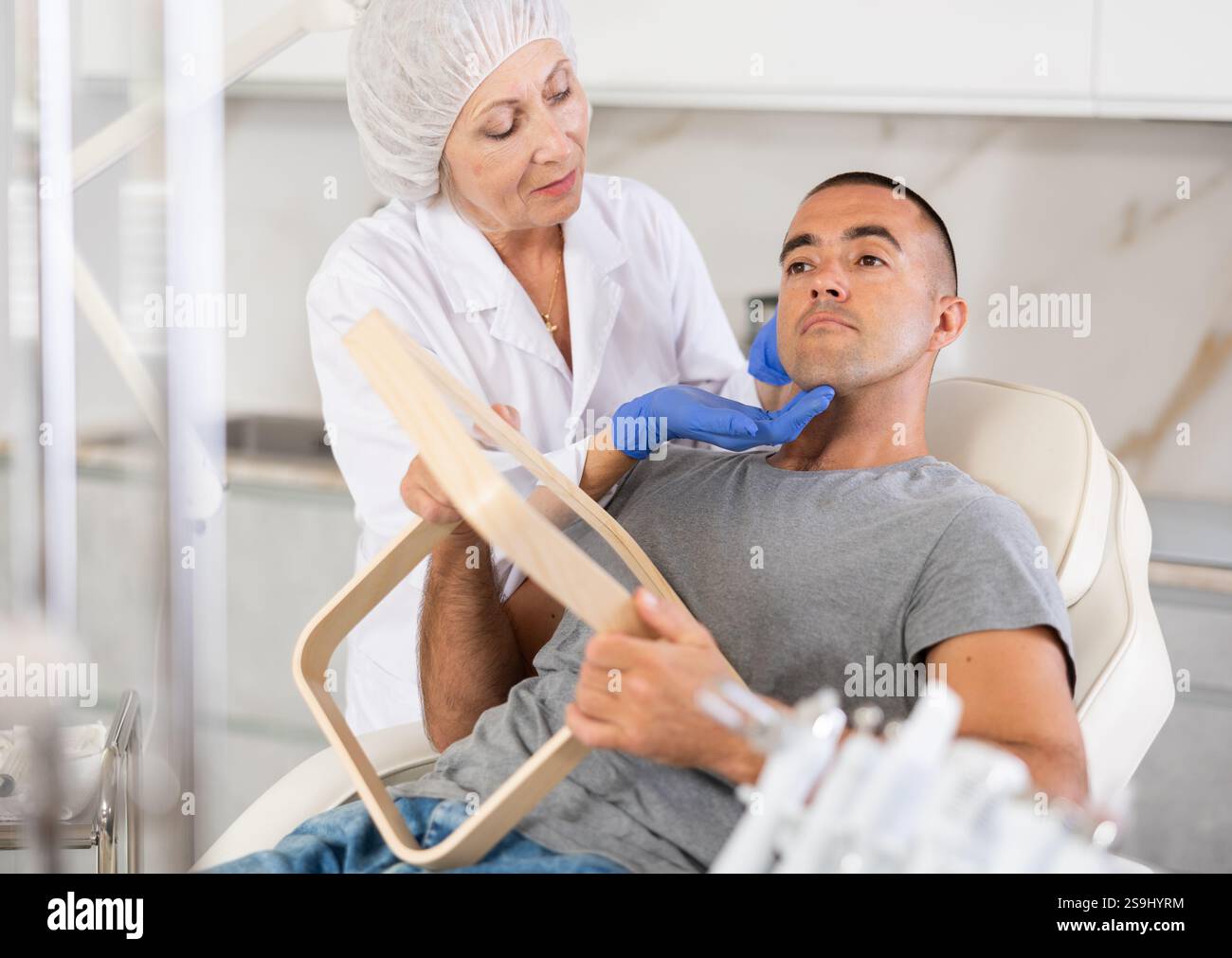 Female doctor, together with male patient, examines face in mirror ...