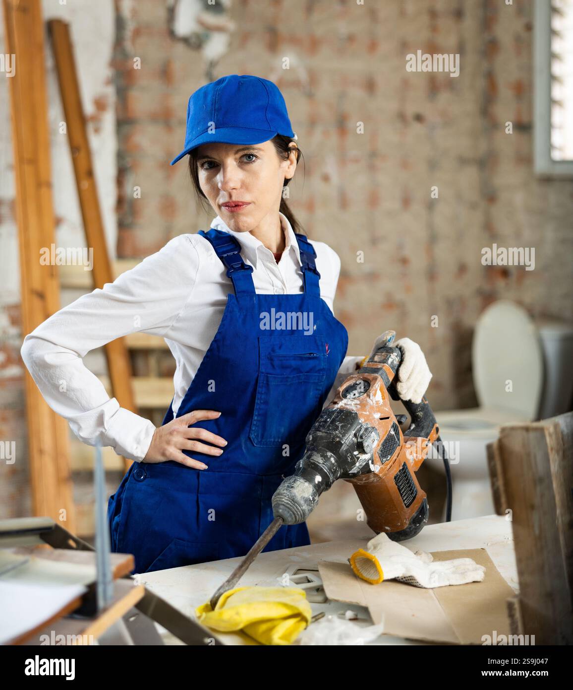 Female contractor standing with demolition hammer inside building under ...