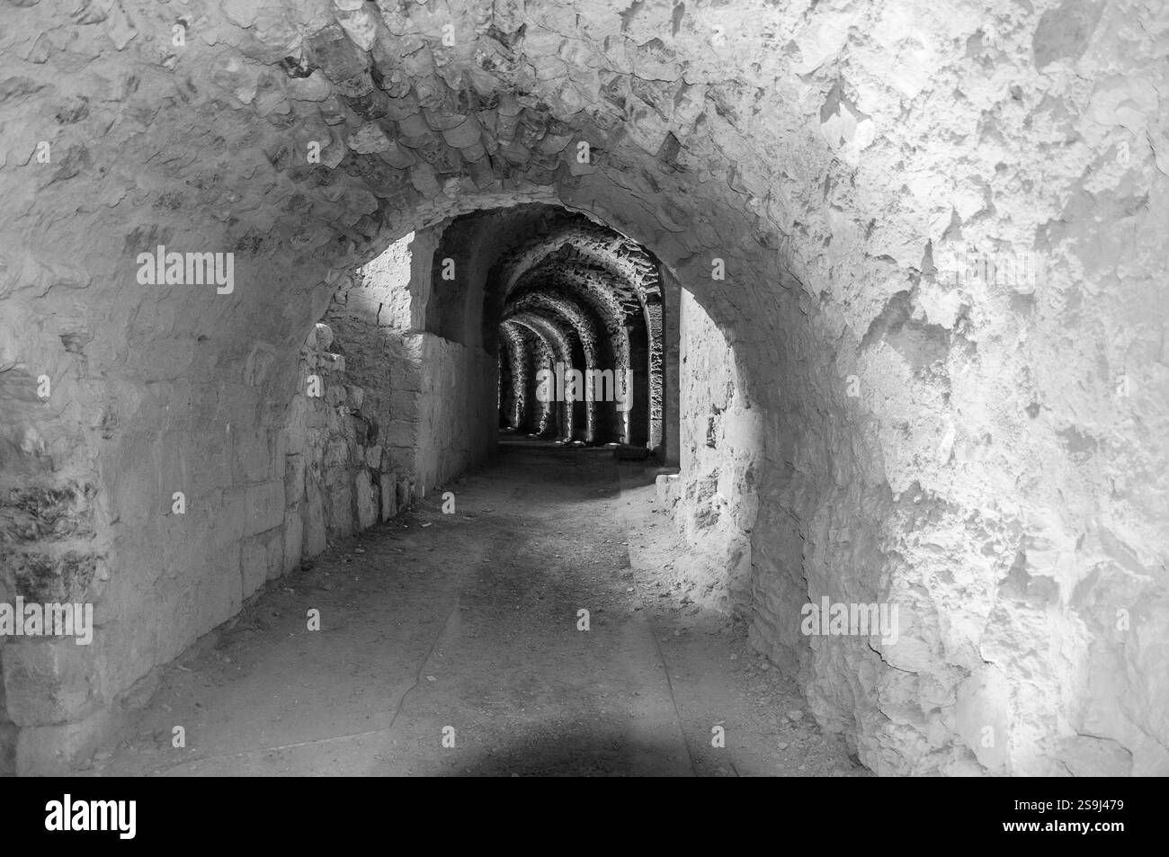 A long, narrow tunnel with a white stone wall. The tunnel is dark and ...