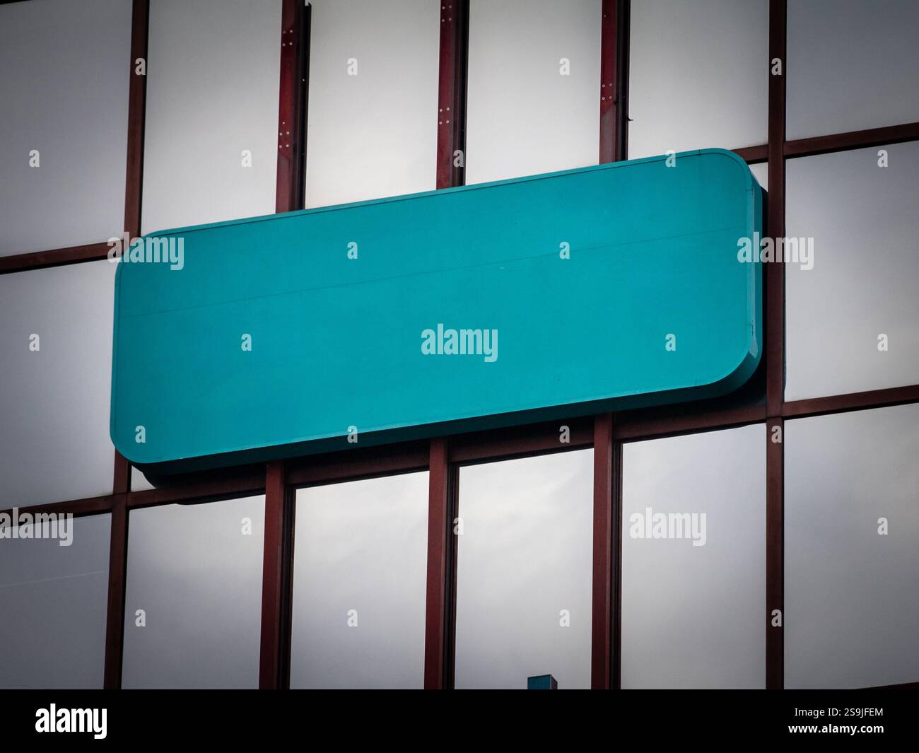 A blank green rectangular sign mounted on a business building’s glass ...
