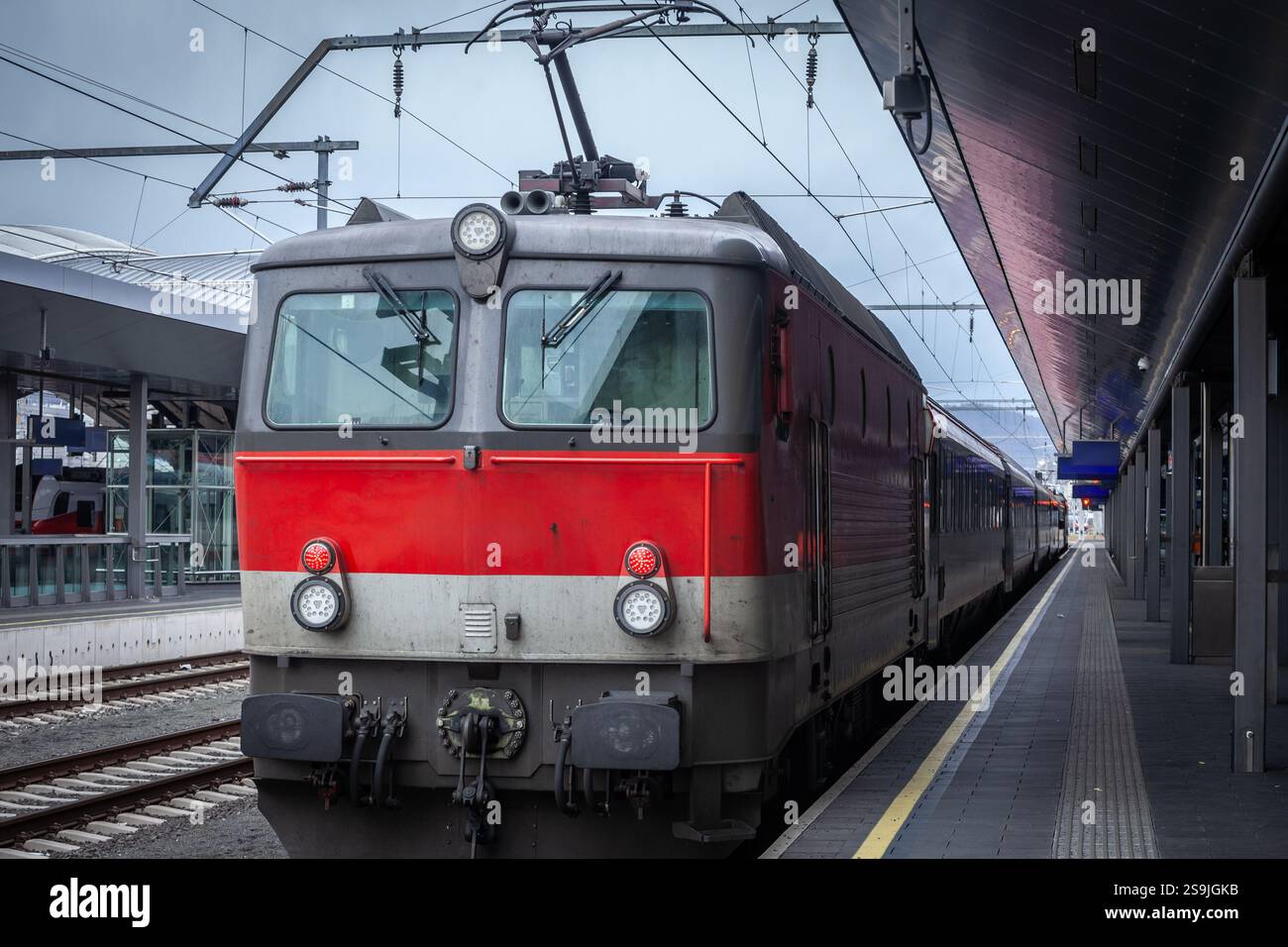 A red passenger train stands poised at Graz Hauptbahnhof, symbolizing ...