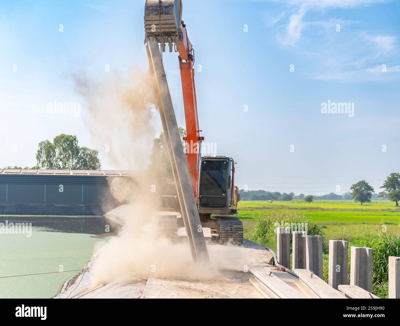 The backhoe is lifting the pile, with dust spreading around the edge of ...