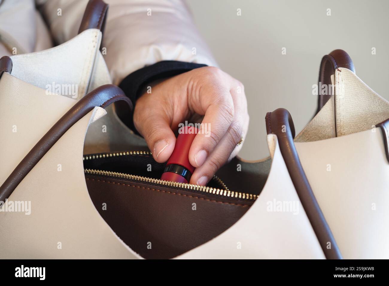 Hand reaching for lipstick tube inside stylish handbag at a cozy indoor ...