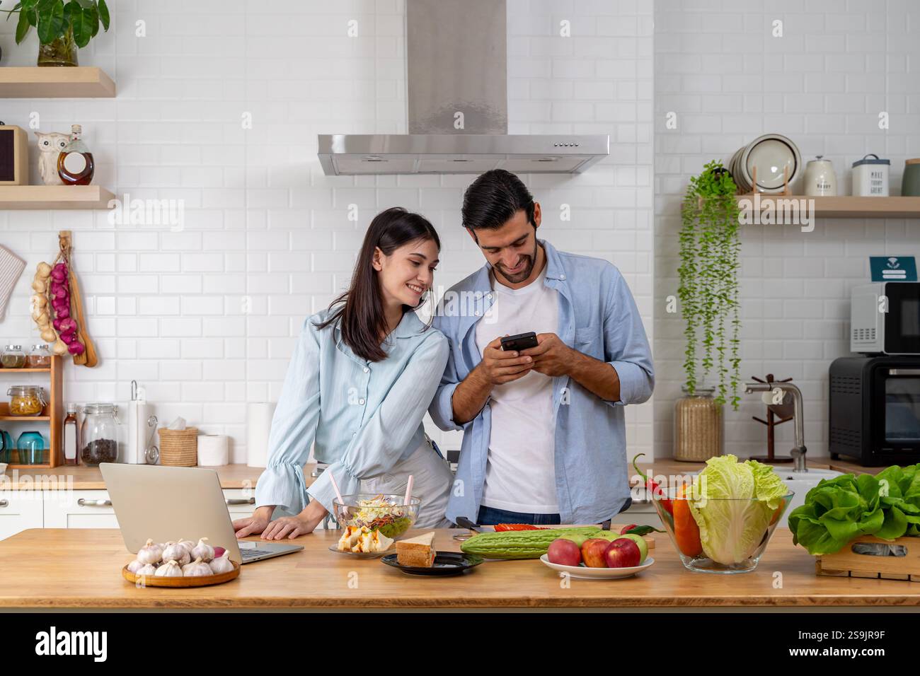 Portrait of young cheerful couple using smartphone and laptop indoors ...