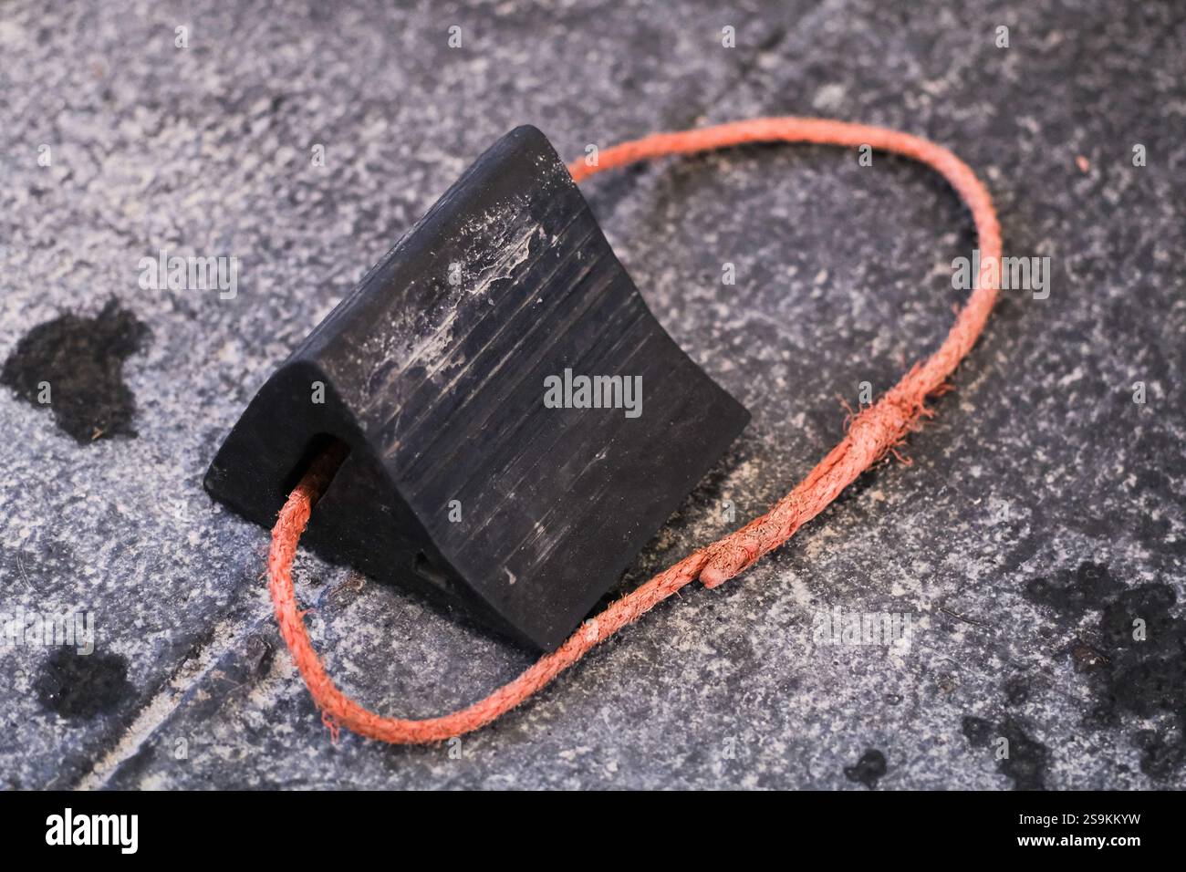 A black plastic wheel stopper with a rope Stock Photo - Alamy