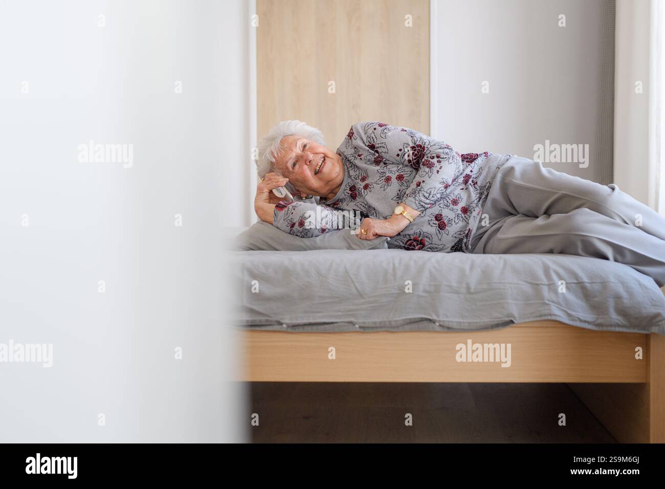 Elderly woman receiving a joyful wake up phone call from friend, lying ...