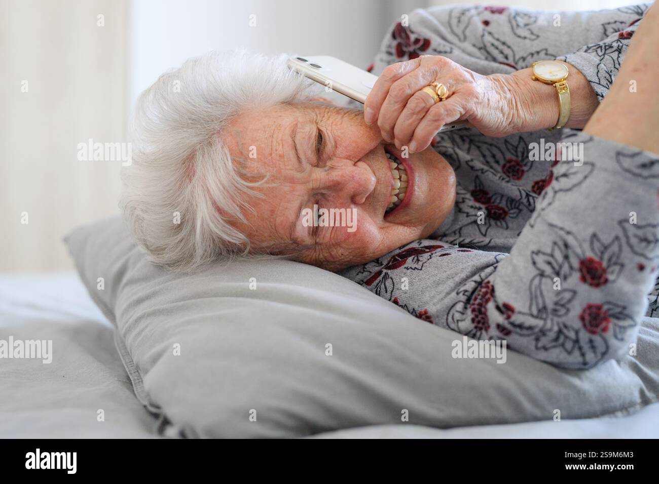 Elderly woman receiving a joyful wake up phone call from friend, lying ...