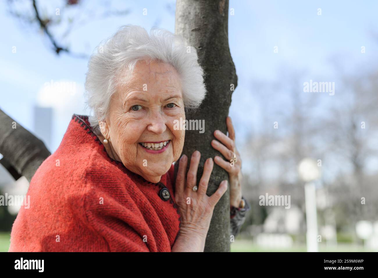 Portrait of lovely elderly woman hugging tree, standing in park. Spring ...