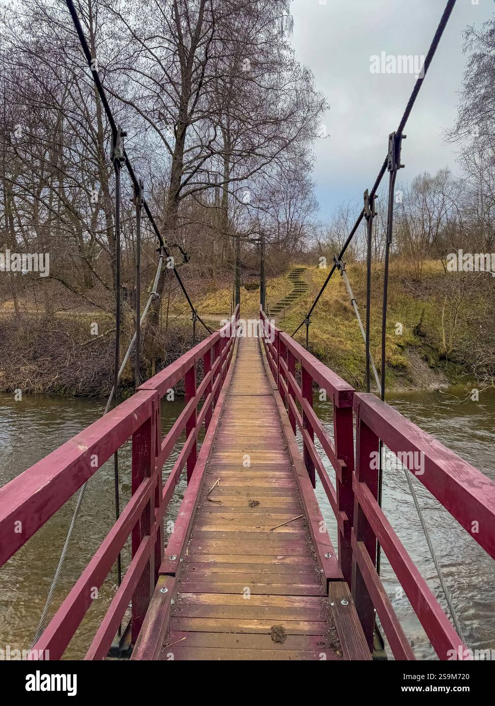 Wooden red old suspension bridge stretches over a flowing river. High ...