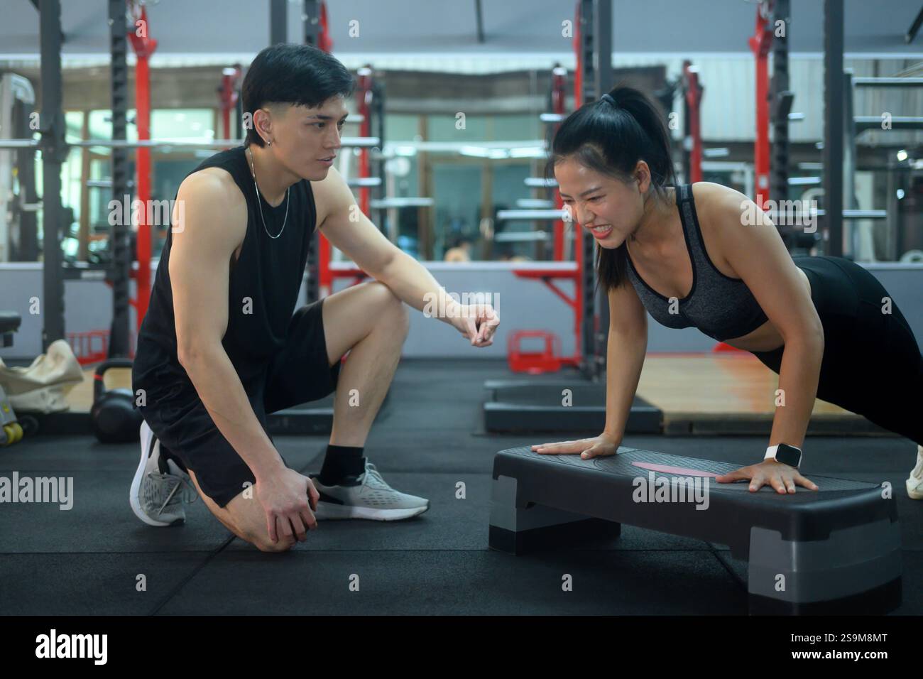 Personal trainer assisting his client during push up exercise on a step ...
