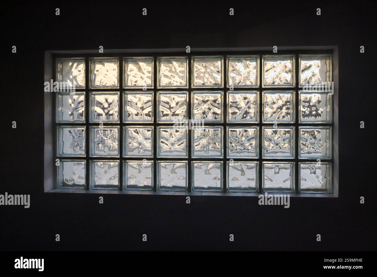 Soft light illuminates a textured glass block window, casting intricate ...