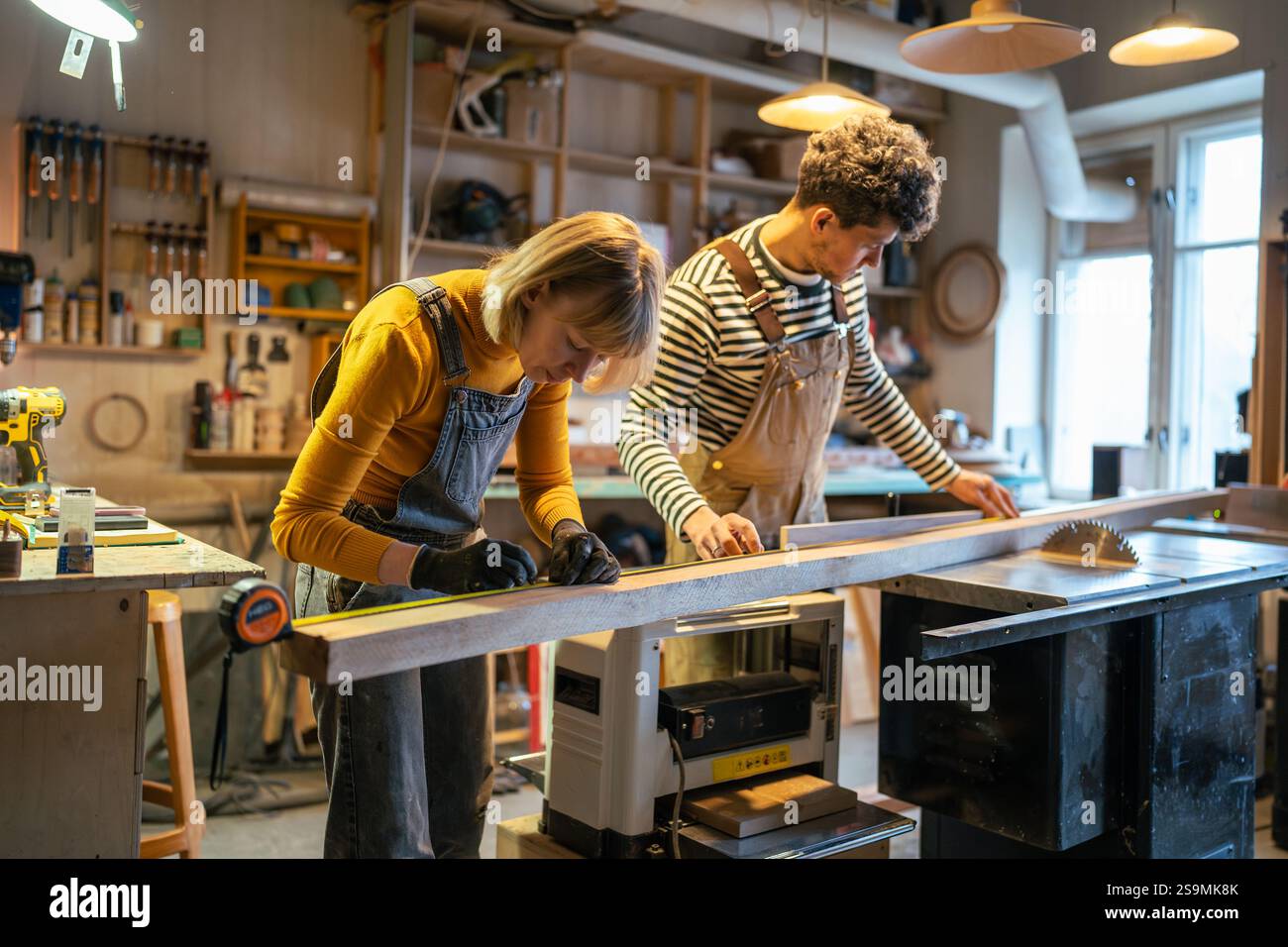 Carpenter pair cutting wooden beams on electric circular saw machine ...