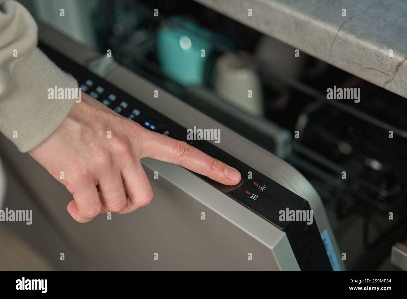Hand pressing start button on dishwasher control panel with open door ...