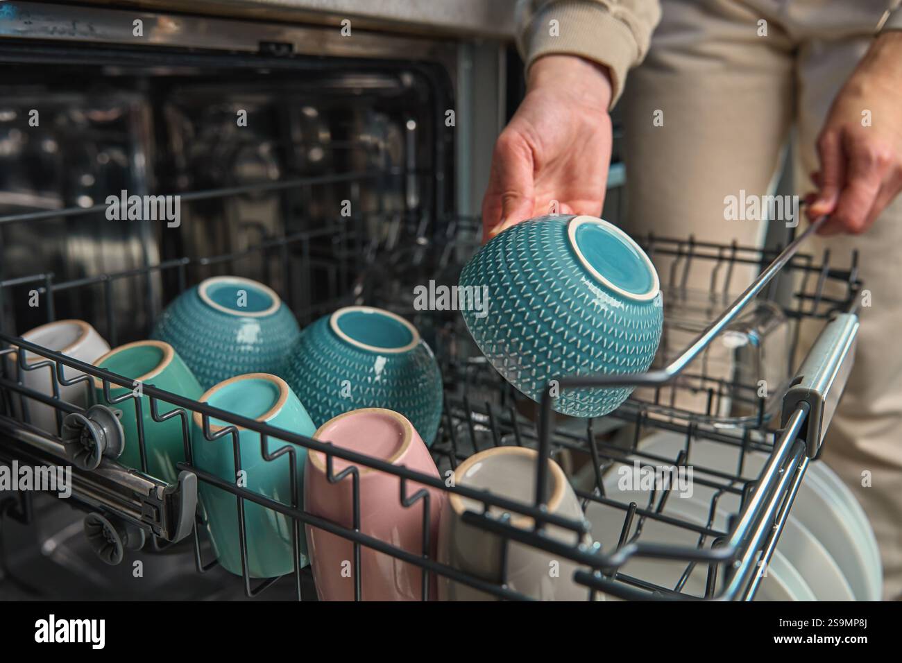 Woman unloading clean dishes and colorful bowl from dishwasher in ...