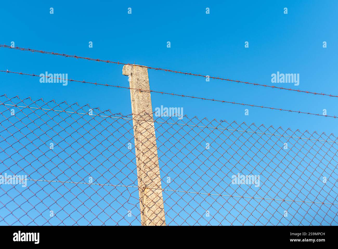 concrete pillar and a wire mesh fence with barbed wire against blue sky ...