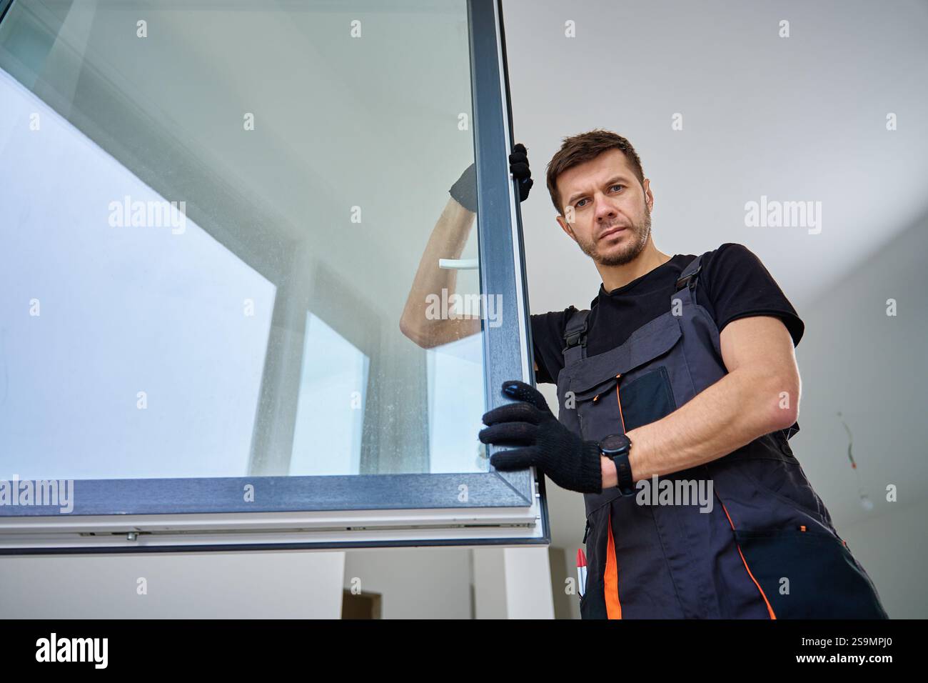 Professional installer in workwear and gloves handling glass window ...