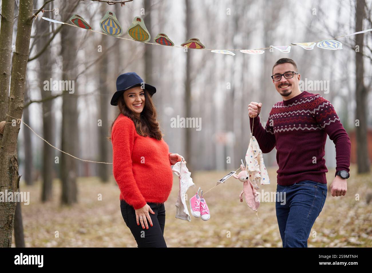 A happy pregnant woman and her husband hanging baby clothes and an ...