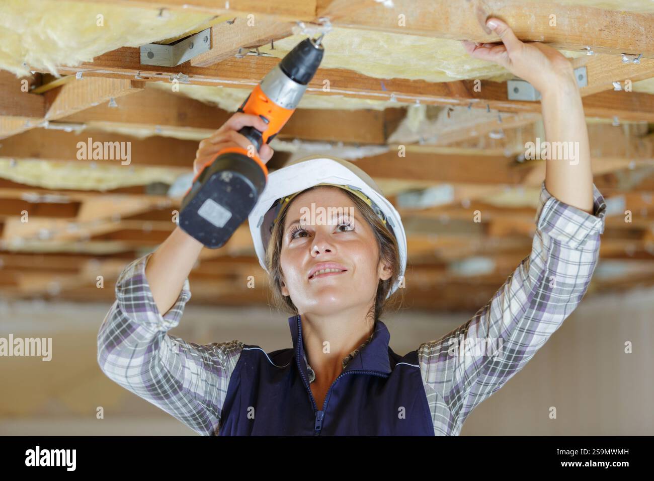 female construction worker using cordless drill on wooden ceiling ...