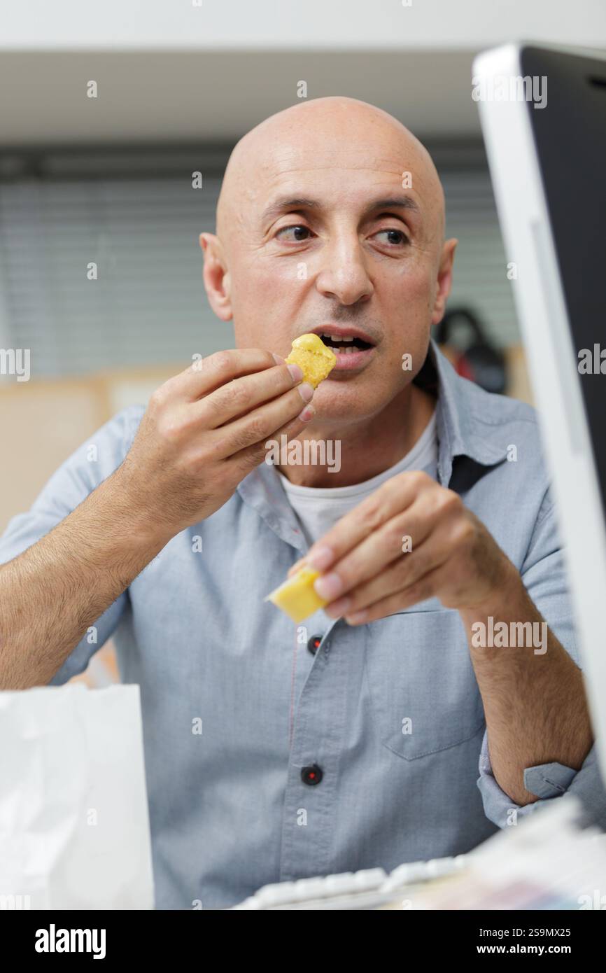 man eating chips in office Stock Photo - Alamy