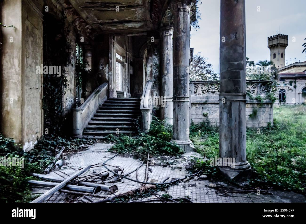 Vines and weeds overtake the crumbling staircase of this abandoned mansion, showcasing decaying ...