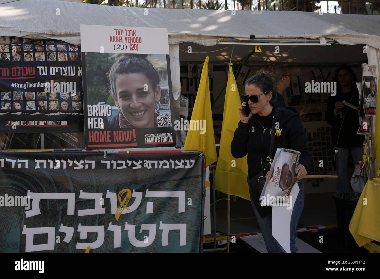 A woman walks past a photo of Arbel Yehoud, and a banner in Hebrew ...