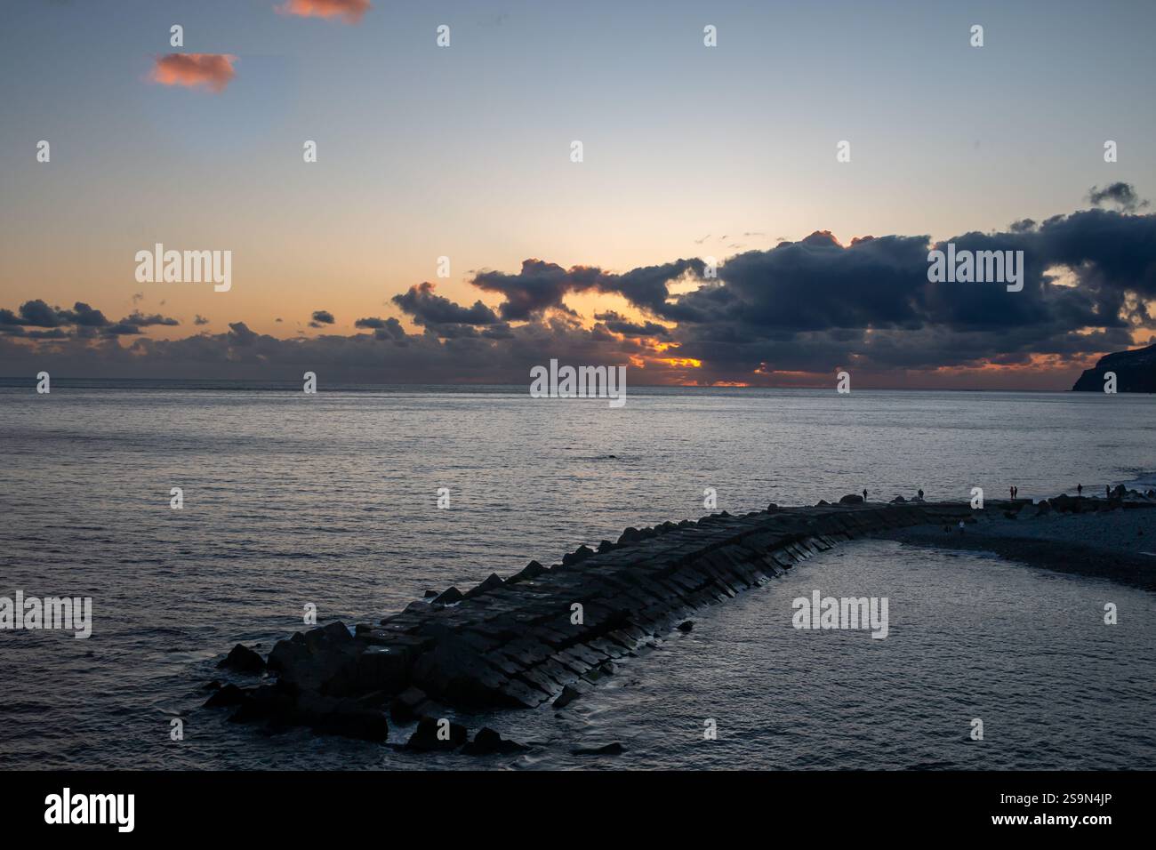 Stone pier and calm Atlantic ocean during a sunset. Dramatic clouds on ...