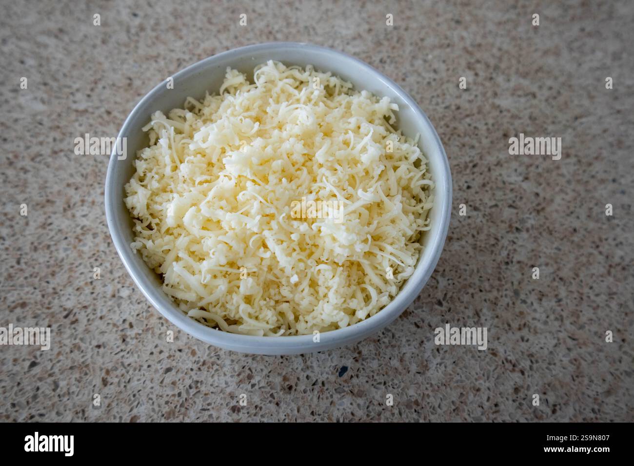 Ceramic white bowl full of shredded white cheese, speckled countertop ...