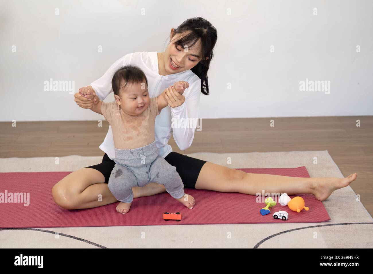 Multitasking mother helping her baby stand up, enjoying playful moments ...