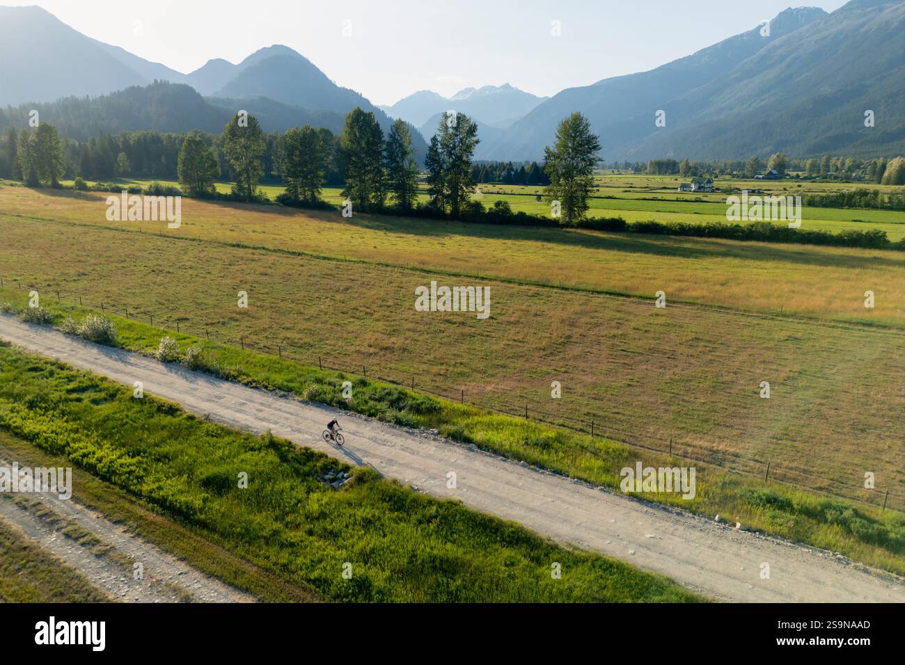 Cyclist on a gravel road in a sunlit rural landscape by mountains Stock ...